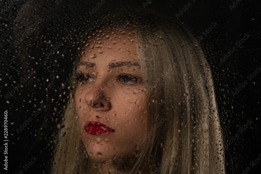 Smooth portrait of crying girl behind glass covered by water drops ...