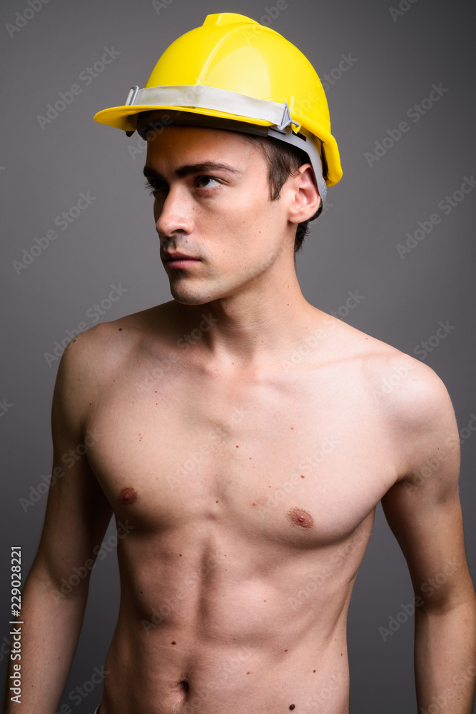 Foto de Handsome sexy man construction worker shirtless against gray ba ...
