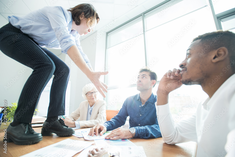 Emotional young woman standing on conference table and gesturing hands ...
