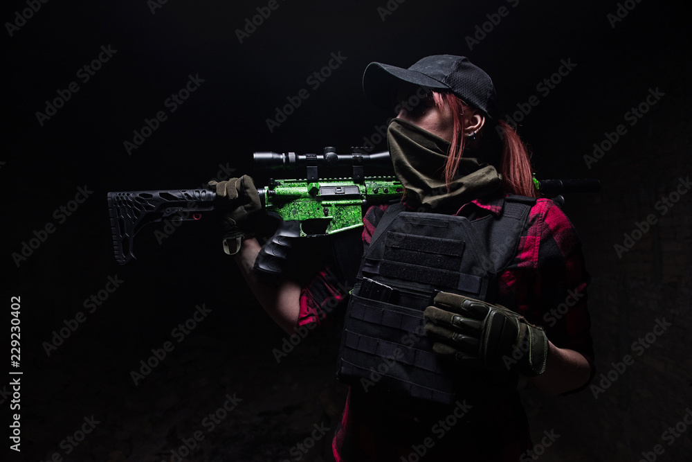 Red-haired girl in black body armor and cap holds sniper rifle on her ...