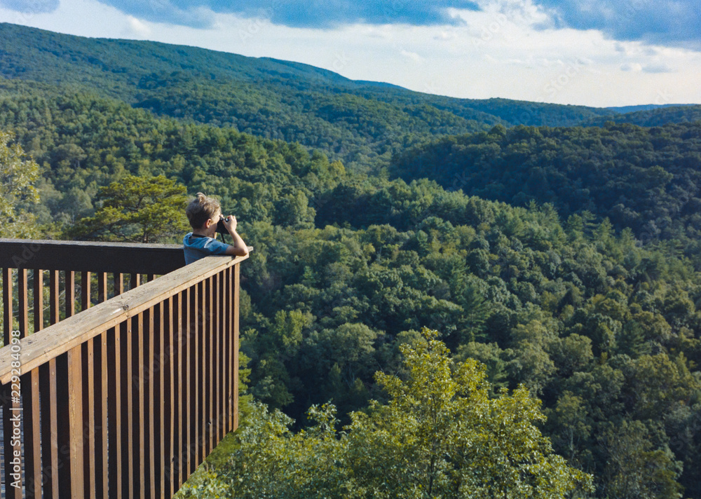 Horizontal medium shot view of a young boy snapping pics from a scenic ...