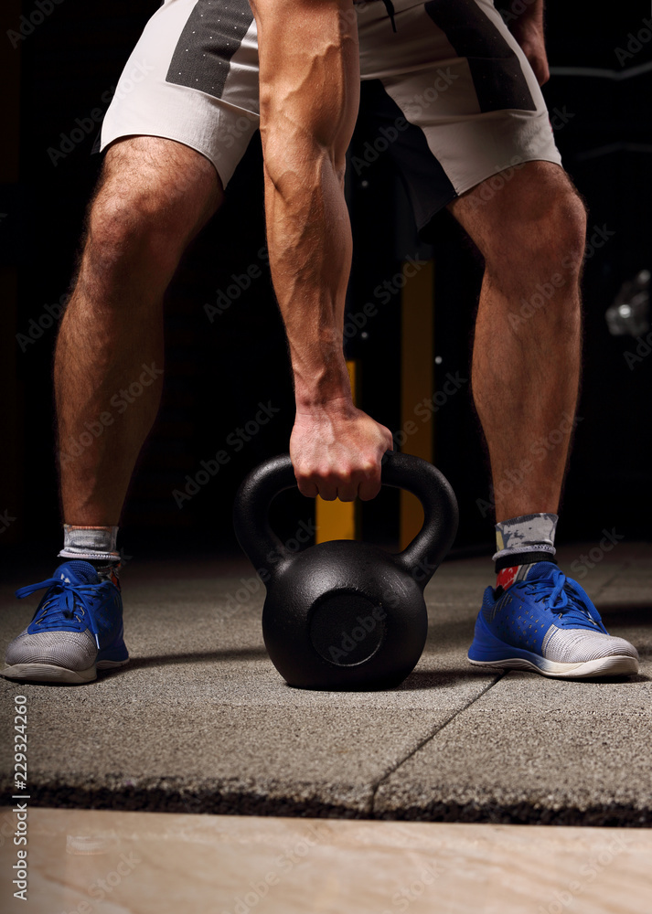 Handsome strong man holding one muscle arm the kettlebell on dark sport ...