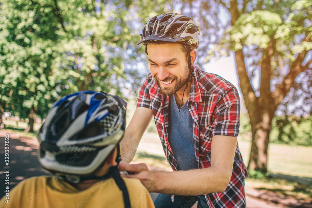 Happy father is looking down at his child and locking his helmet. They ...