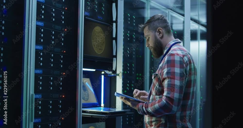 Side view of modern IT engineer using tablet and laptop setting servers ...