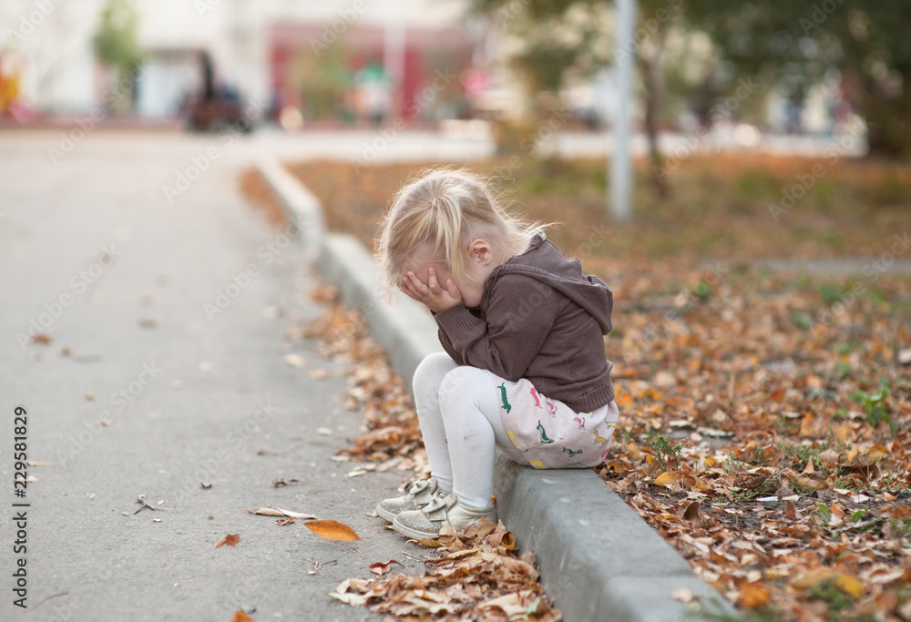 Lost girl in the city. Sad baby girl sitting on the curb and holding ...