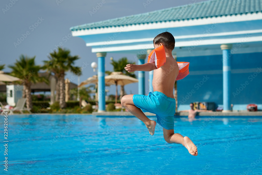 Caucasian boy having fun making high jump to plunge into swimming pool ...