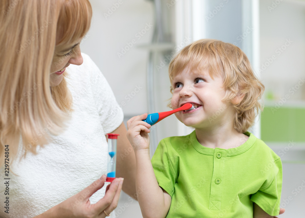 Kid boy brushing his teeth in bathroom. His mother monitoring accuracy ...