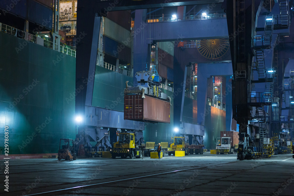 Large mooring crane unloads container ship at night. Container terminal ...