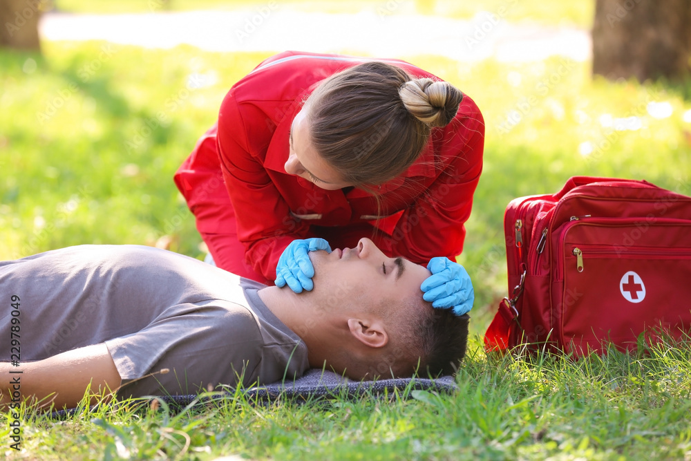 Woman in uniform checking for breathing of unconscious man outdoors ...