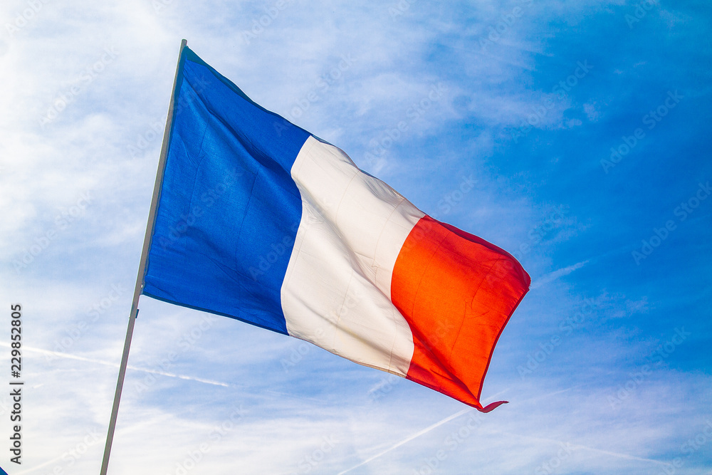 French flag waving on the pole on a blue sky with clouds during a ...