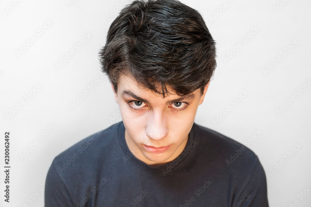 A sad boy on a white background looks up. He had an angry look because ...
