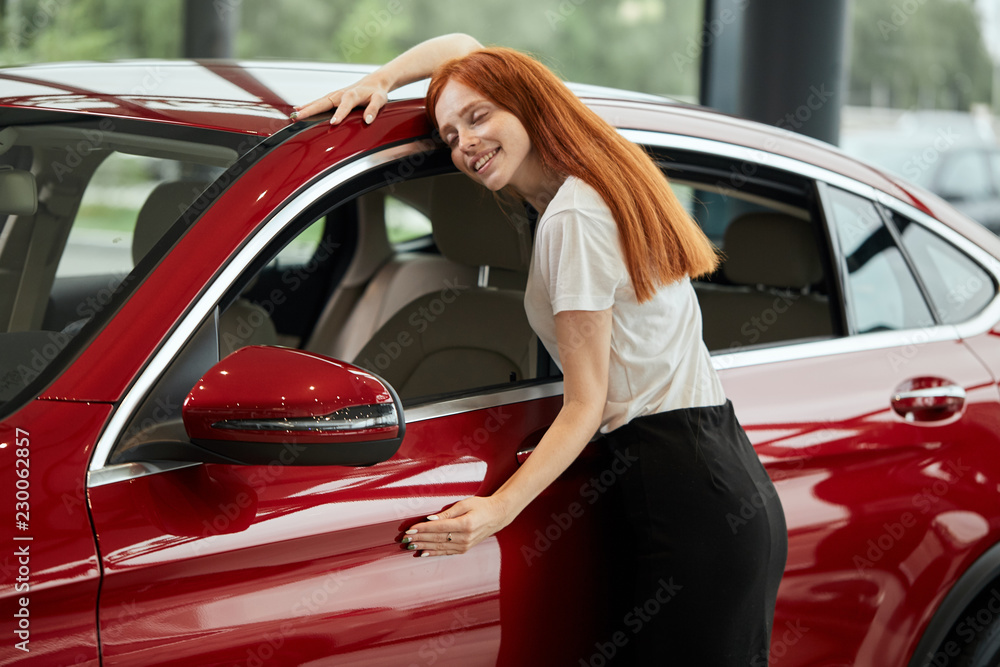 Emotional young woman embracing her new automobile at the dealership ...