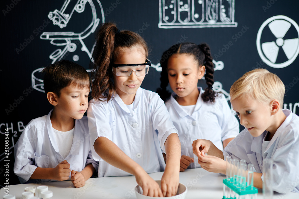 Multiethnic group of 7 years old kids in white lab coats doing a ...