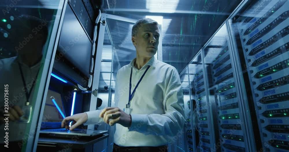 Wide shot of technician working on a laptop in a data center full of ...