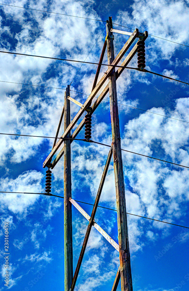High voltage power lines on wooden poles with cloudy sky background ...