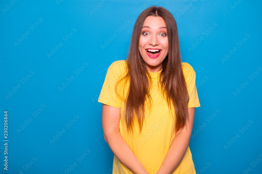 Cute brunette woman with long hair posing in yellow t-shirt on a blue ...