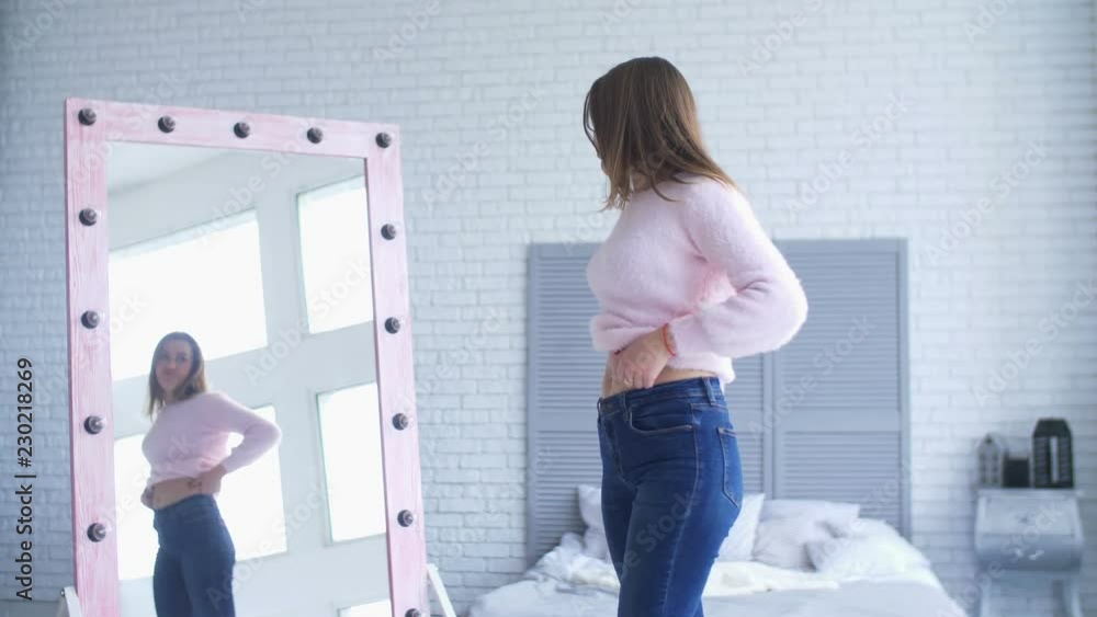 Sad depressed attractive woman in trendy clothes checking her body shape in mirror, displeased ...