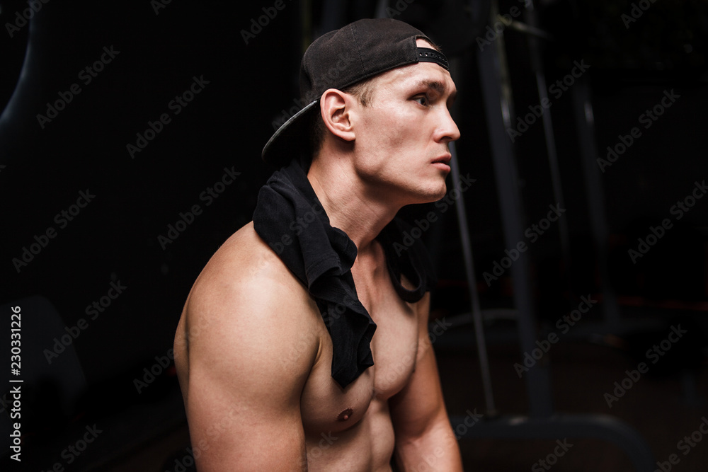 Muscular, shirtless young man resting in gym during workout, showing ...