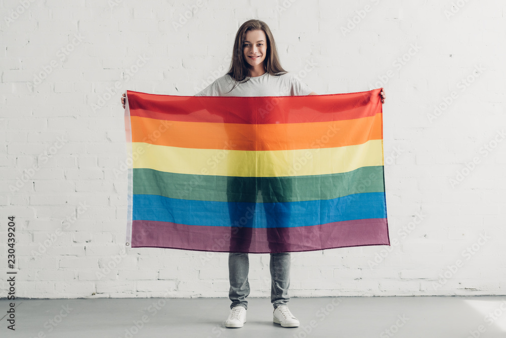 Foto de young transgender woman holding pride flag in front of white ...