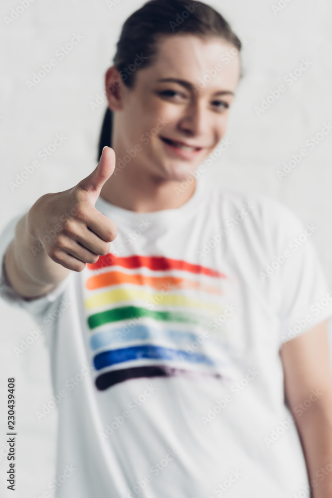 young transgender woman in white t-shirt with pride flag showing thumb ...