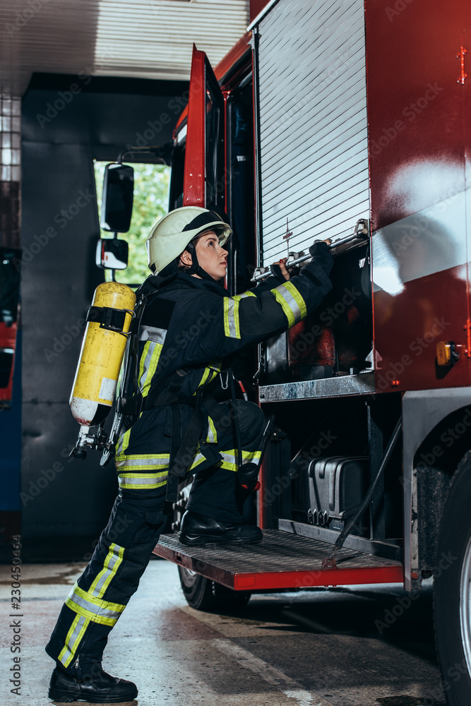 side view of female firefighter with fire extinguisher on back closing ...