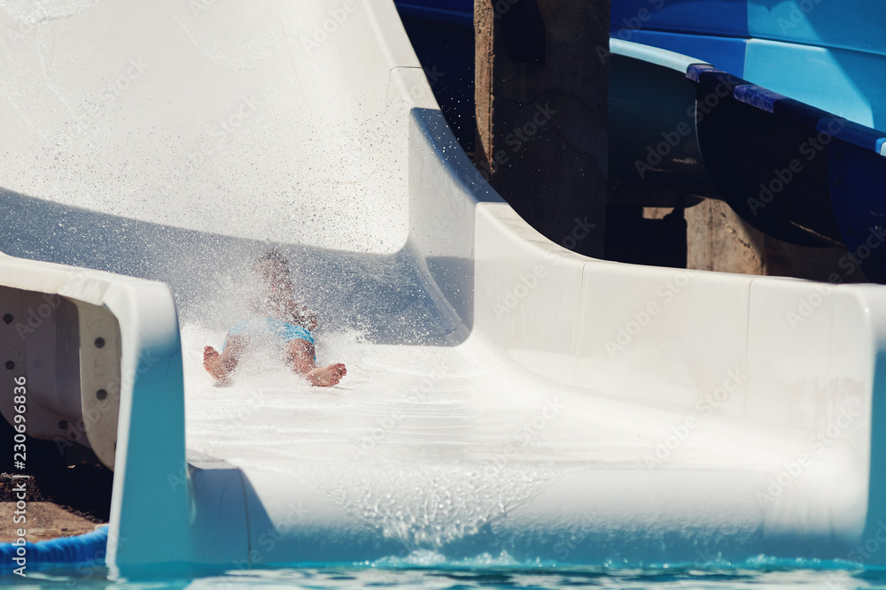 Boy is gliding down the white water slide in the waterpark. There are a ...