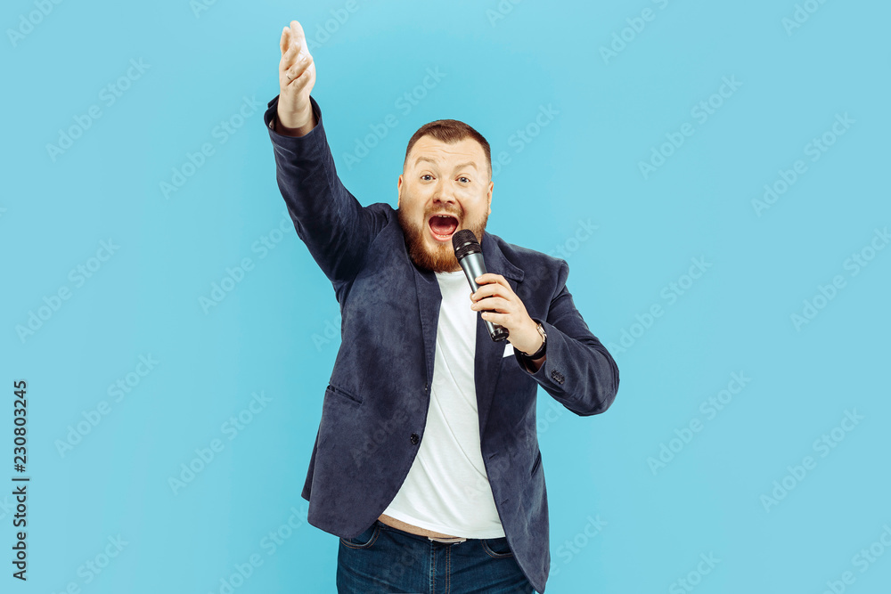 Young man with microphone on blue studio background, leading concept ...