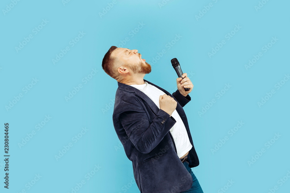 Young man with microphone on blue studio background, leading concept ...