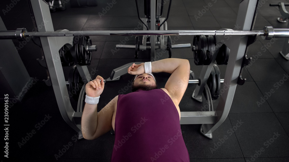 Fat man wipes forehead, tired after lifting up barbell, exhausting ...