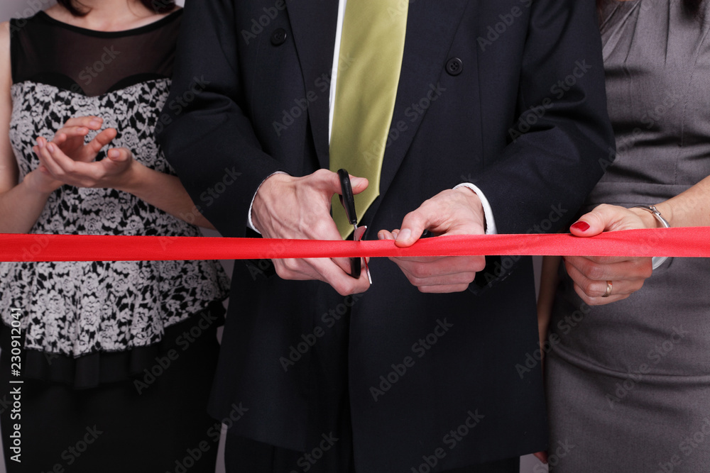 Businessman cutting red ribbon while other people next to him are ...