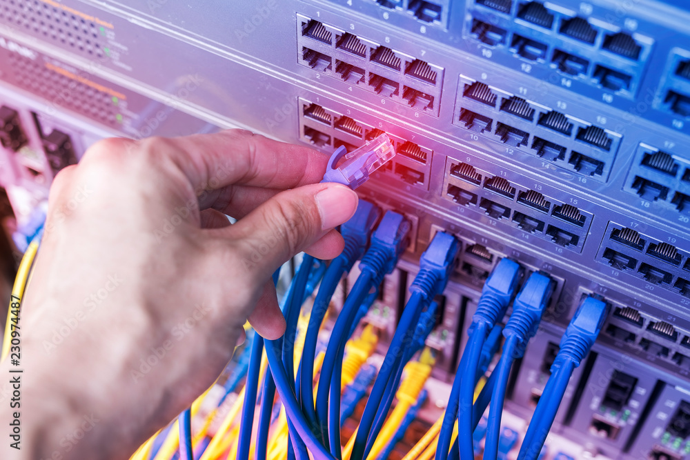 man working in network server room with fiber optic hub for digital ...