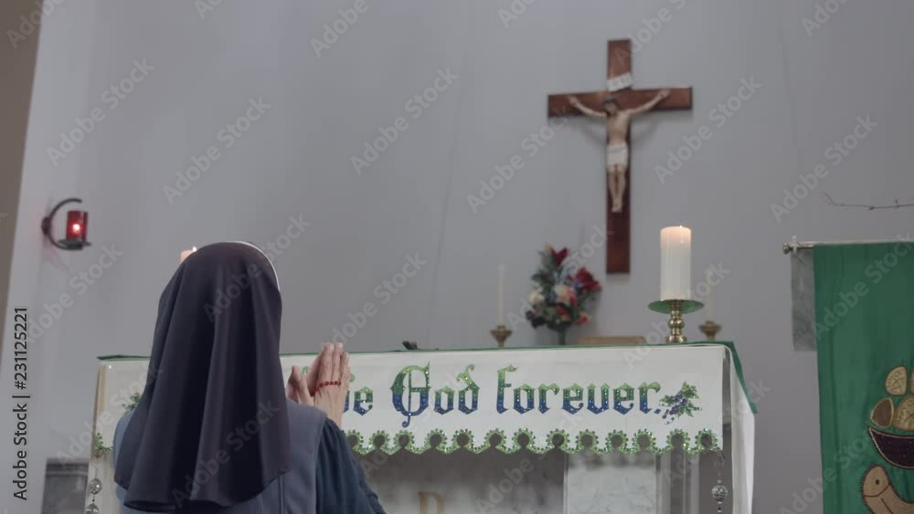 Religious sister praying and kneeling in front of altar with crucifix ...