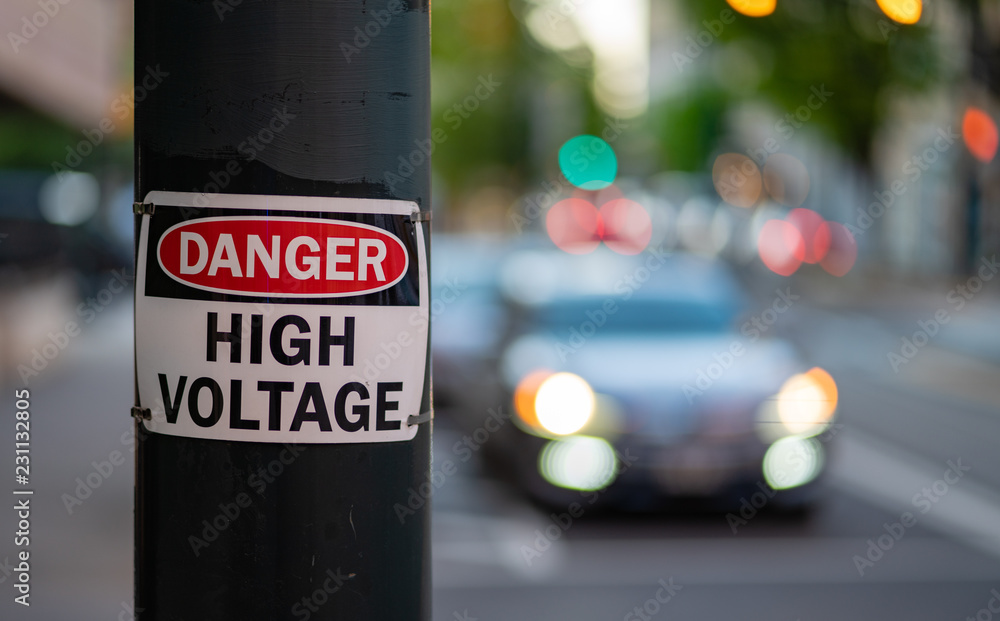 A high voltage warning sign hanging on a single power pylon, blurry ...