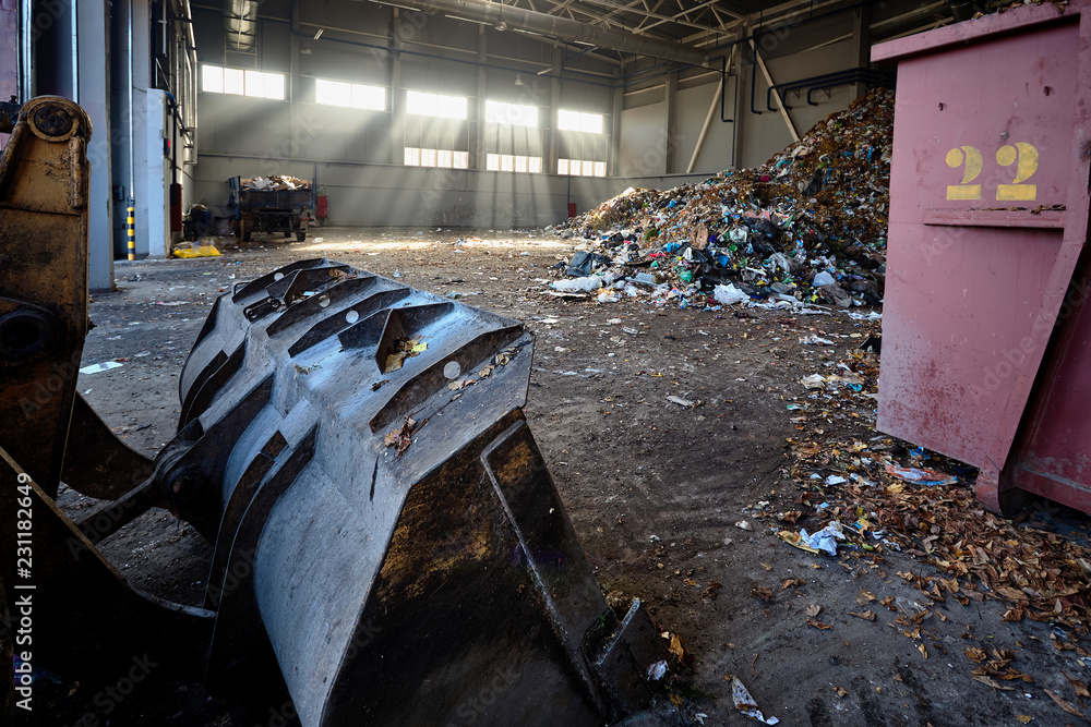 Heavy bulldozer bucket in rays of evening sun in building of waste ...