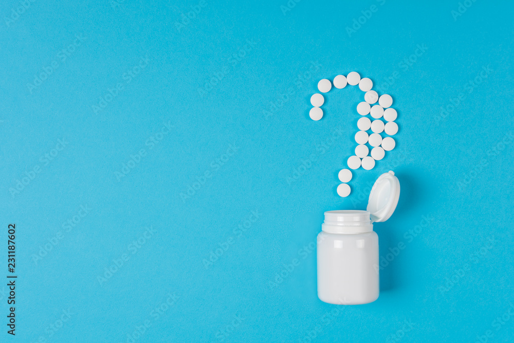 White pills in a question mark poured from a medicine bottle on blue ...