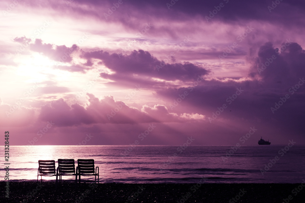 Seascape with heavenly light rays and three chairs on the beach in ...