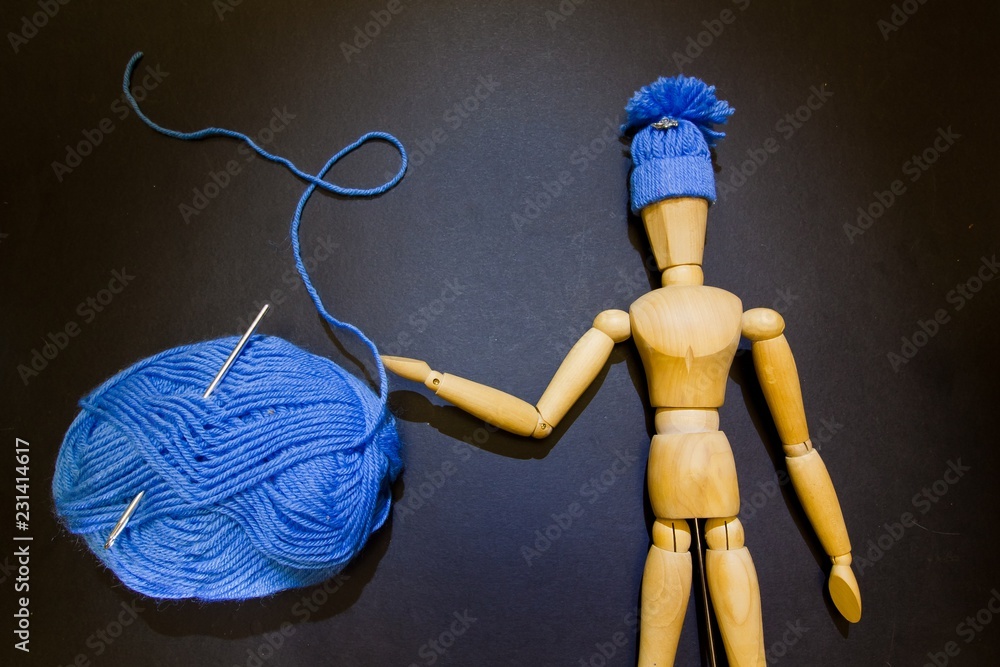 Wooden puppet wears a blue knitted winter hat and points aside with its ...