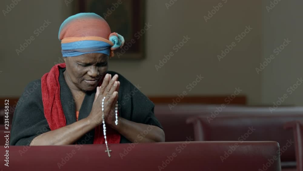 An African woman, wearing a colourful head scarf, kneeling and praying ...