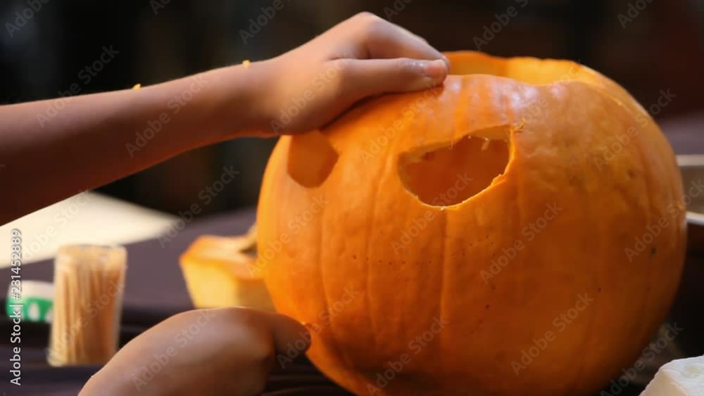 The hands of a young girl mark a pumpkin for carving by poking holes ...