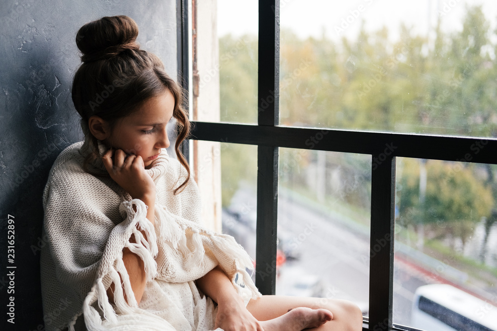 Foto de Pensive caucasian girl with sad emotions sitting on sill ...