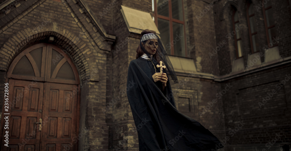 Young nun is standing and praying with cross in her hands on temple ...