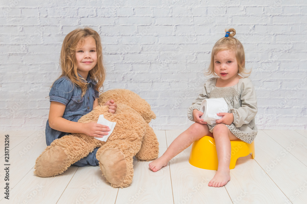 against the background of a white brick wall, the girl sits on a potty ...