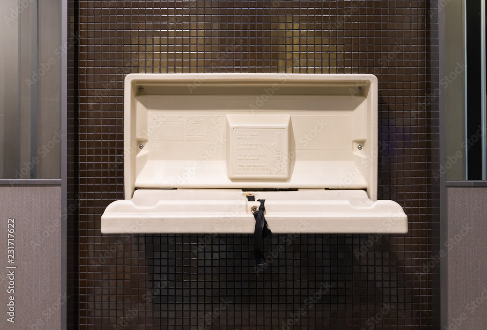 white plastic diaper table on brown ceramic wall in toilet. Baby diaper ...
