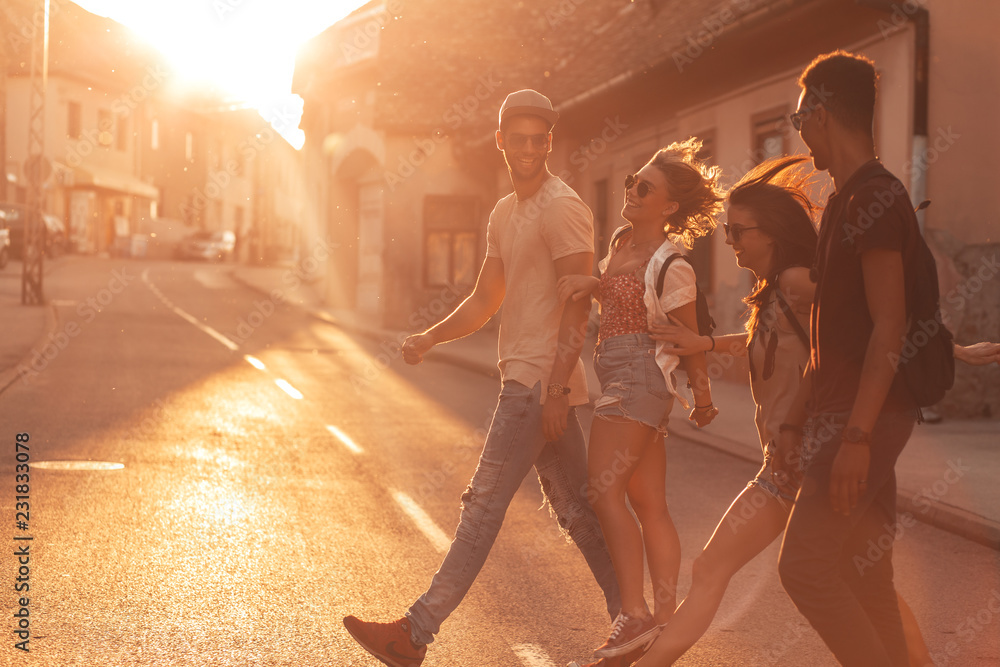 Group of friends walking and laughing at the city street at sunset ...