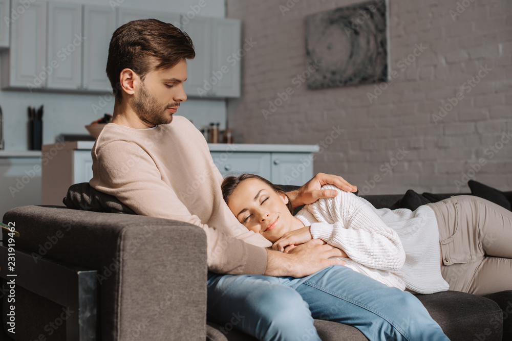 handsome young man sitting on couch while his girlfriend sleeping on ...