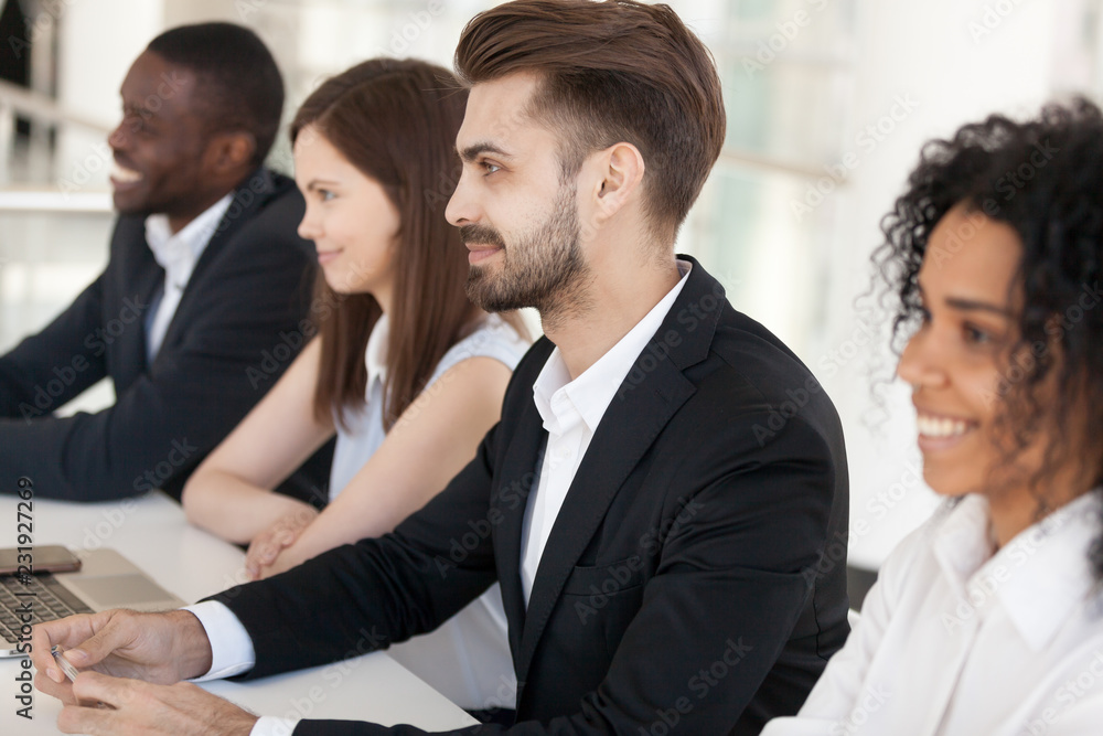 Diverse millennial employee sit in row at table looking at presenter or ...