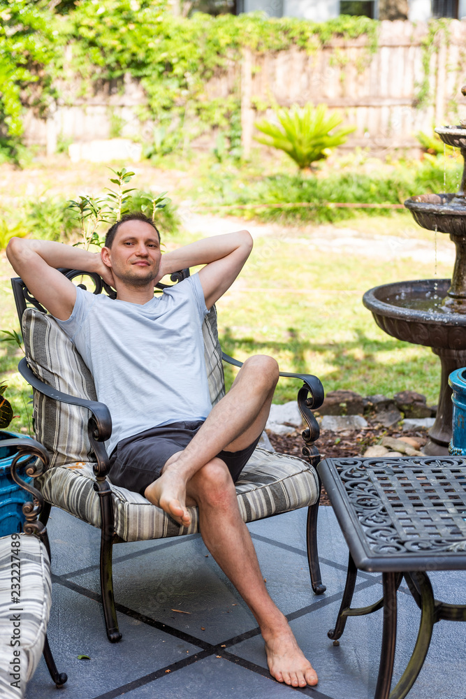Young happy man sitting on patio lounge chair in outdoor spring flower ...