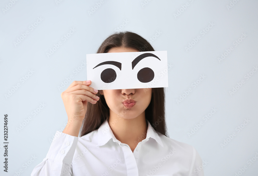 Emotional young woman hiding face behind sheet of paper with drawn eyes ...