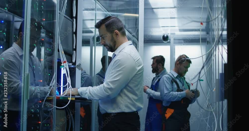 Medium shot of three people working in a data center with cable to ...