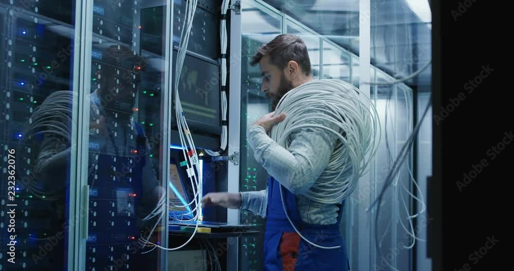 Medium shot of a male technicians working in a data center carrying ...